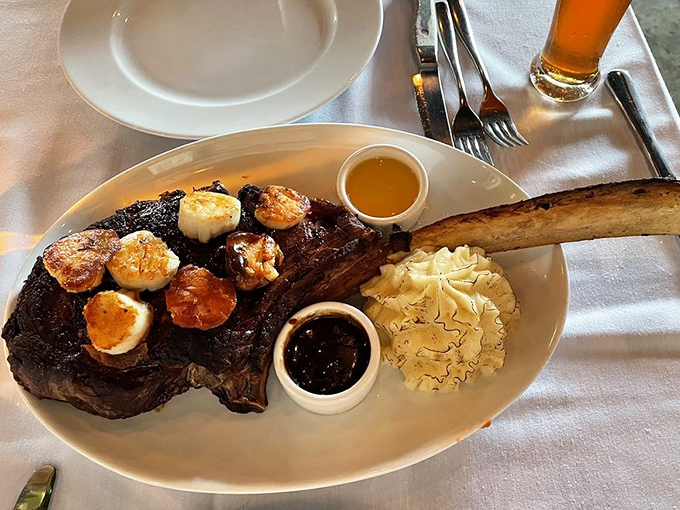 The tomahawk steak arrives like a prehistoric indulgence, topped with scallops because sometimes too much is exactly enough.