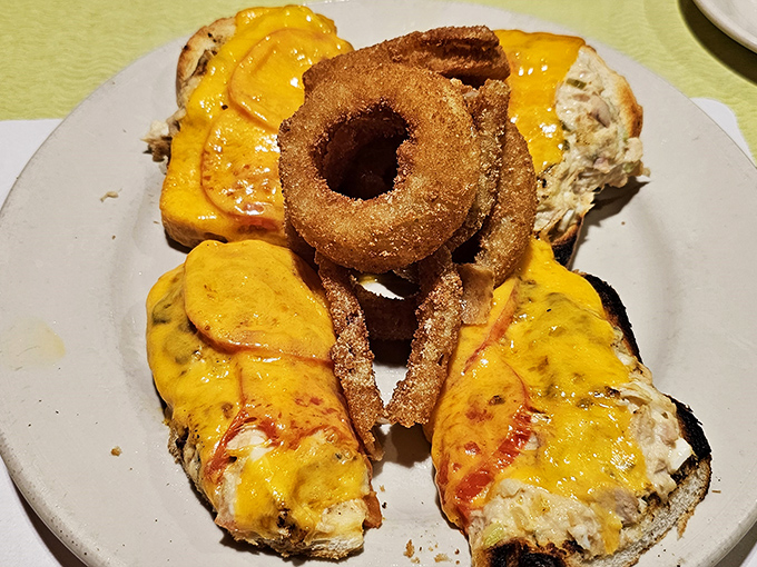 A sandwich architect's masterpiece—melted cheese cascading over perfectly grilled bread with onion rings standing guard. This isn't lunch; it's an edible achievement.