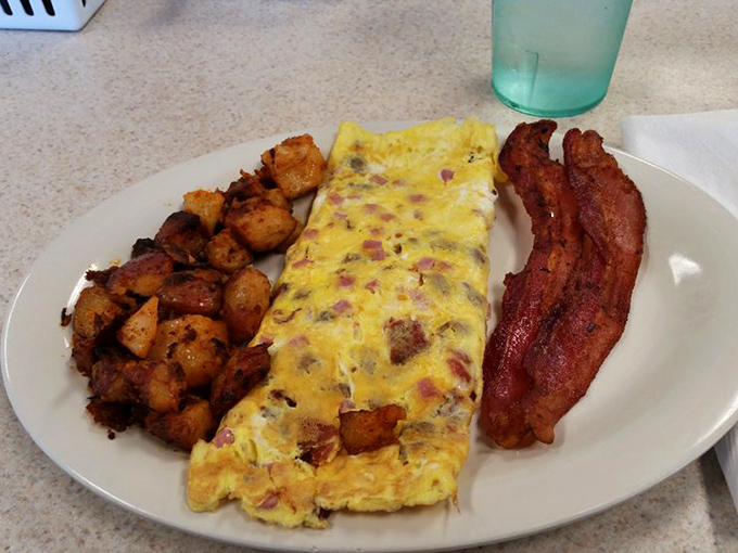 The holy breakfast trinity: perfectly seasoned home fries, a folded omelet bursting with fillings, and bacon that's achieved that mythical balance between crisp and chewy.