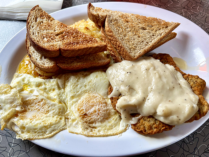 Breakfast perfection on a plate: sunny-side up eggs, golden toast, and country fried steak smothered in gravy that could make a vegetarian reconsider.