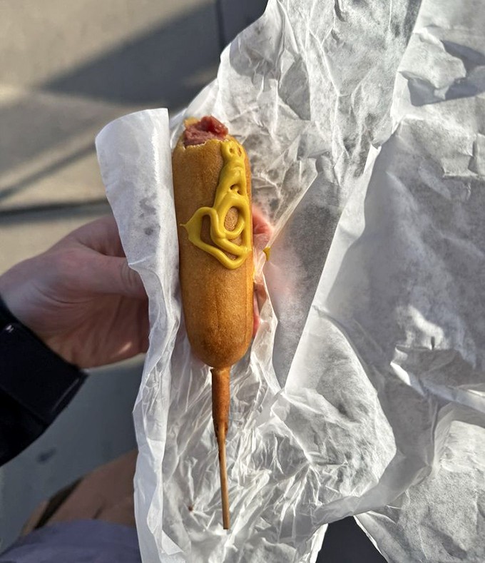 The corn dog &ndash; childhood nostalgia on a stick, elevated to art form with that perfect mustard zigzag that says "I may be simple, but I'm not basic."
