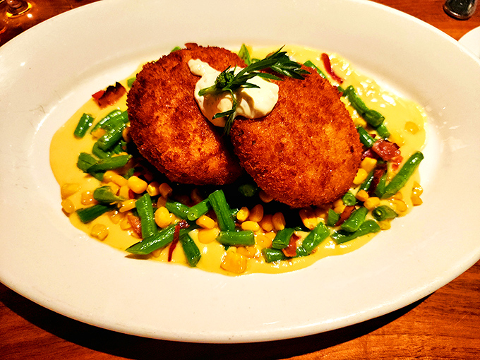 Crab cakes that are actually crab, not breadcrumbs with a seafood rumor, served on a bed of colorful vegetables and corn.