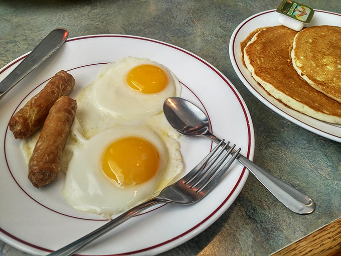The breakfast trinity: perfectly sunny-side-up eggs, sausage links with that satisfying snap, and pancakes golden as a South Dakota sunrise.