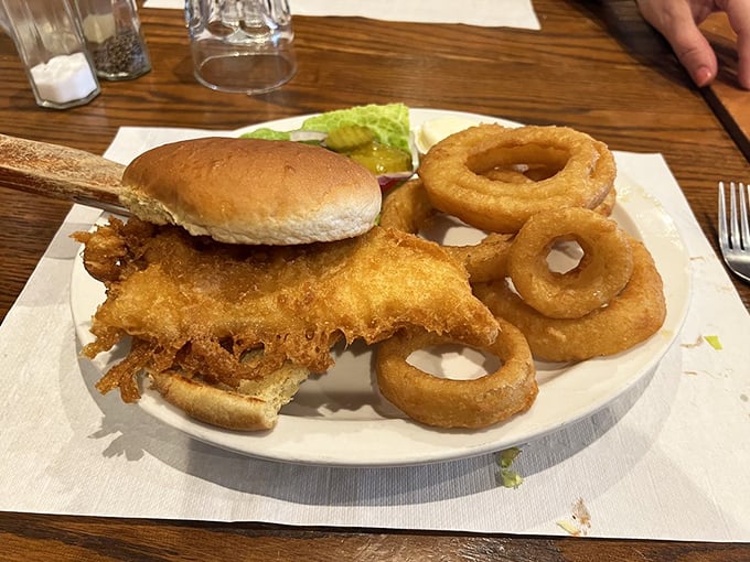 The fish sandwich arrives with golden-battered perfection, crispy onion rings, and the quiet confidence of something that knows exactly what it is. 