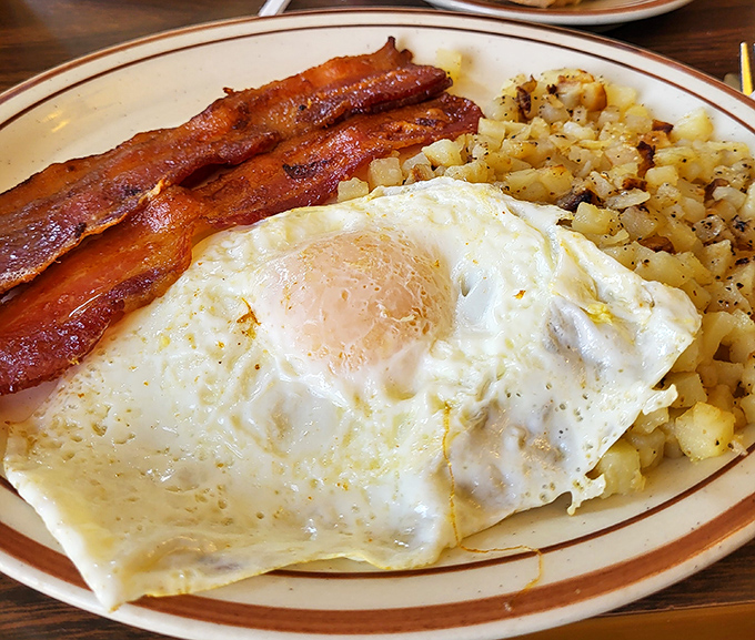 The breakfast trifecta: perfectly crisp bacon, eggs with that ideal runny yolk, and home fries that didn't come from a freezer bag.