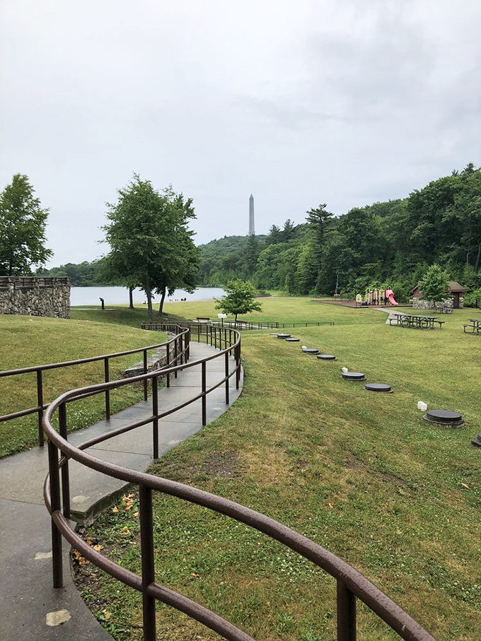 A gently curving pathway invites visitors to the lake and picnic area. The monument plays peekaboo in the distance, visible through summer's green canopy.