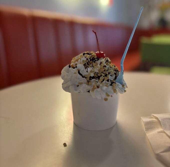 This sundae isn't just dessert—it's architecture. Whipped cream mountain, cherry summit, and that spoon standing at attention like a flagpole.