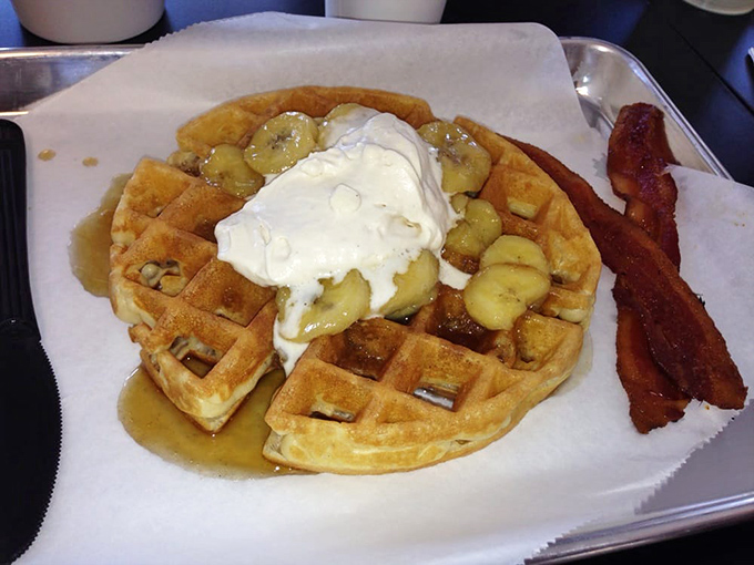 Breakfast nirvana: a golden waffle crowned with caramelized bananas and whipped cream, with bacon standing guard against too much sweetness.