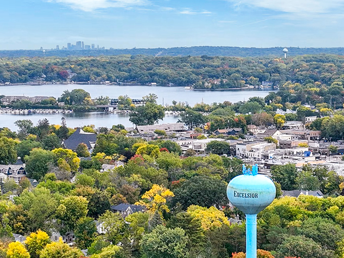 The blue Excelsior water tower rises above treetops, with Lake Minnetonka and the Twin Cities skyline creating a perfect backdrop.