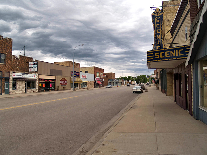 The Scenic theater sign pierces dramatic clouds like a lighthouse, guiding entertainment seekers through any weather storm.