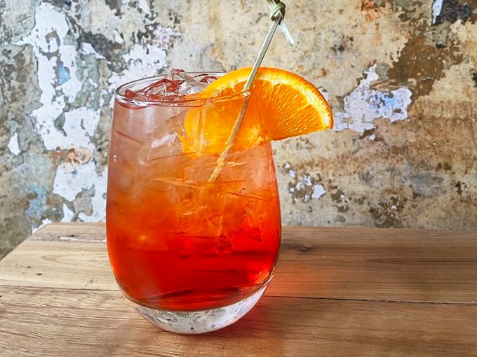 That vibrant Aperol spritz isn't just a drink; it's summer in a glass, perfectly positioned against the restaurant's characterful weathered walls.