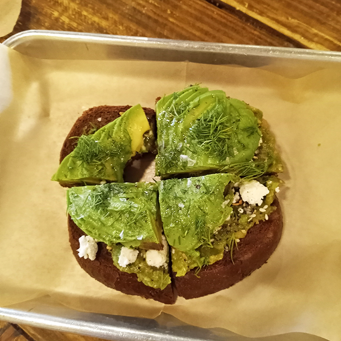 Avocado toast that's actually worth the millennial jokes &ndash; perfectly ripe slices on dark bread with what appears to be feta crumbles and fresh herbs.