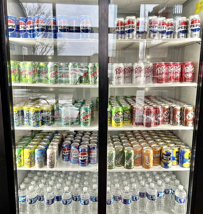 The beverage cooler stands ready, a colorful battalion of thirst-quenchers waiting to combat the pleasant heat of pepperoni and hot honey.