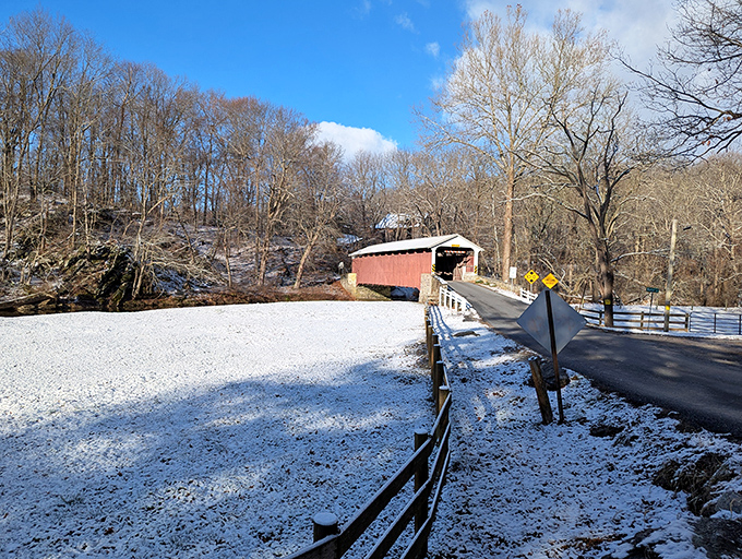 The stark beauty of winter brings a different character to the bridge, with snow creating a pristine backdrop for its weathered red boards.