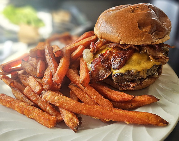 Burger architecture that deserves its own blueprint. Melted cheese cascading over bacon and beef with sweet potato fries standing guard.