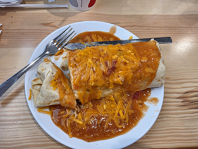 This breakfast burrito arrives smothered in cheese and sauce, looking like it just won the lottery and wants to share.
