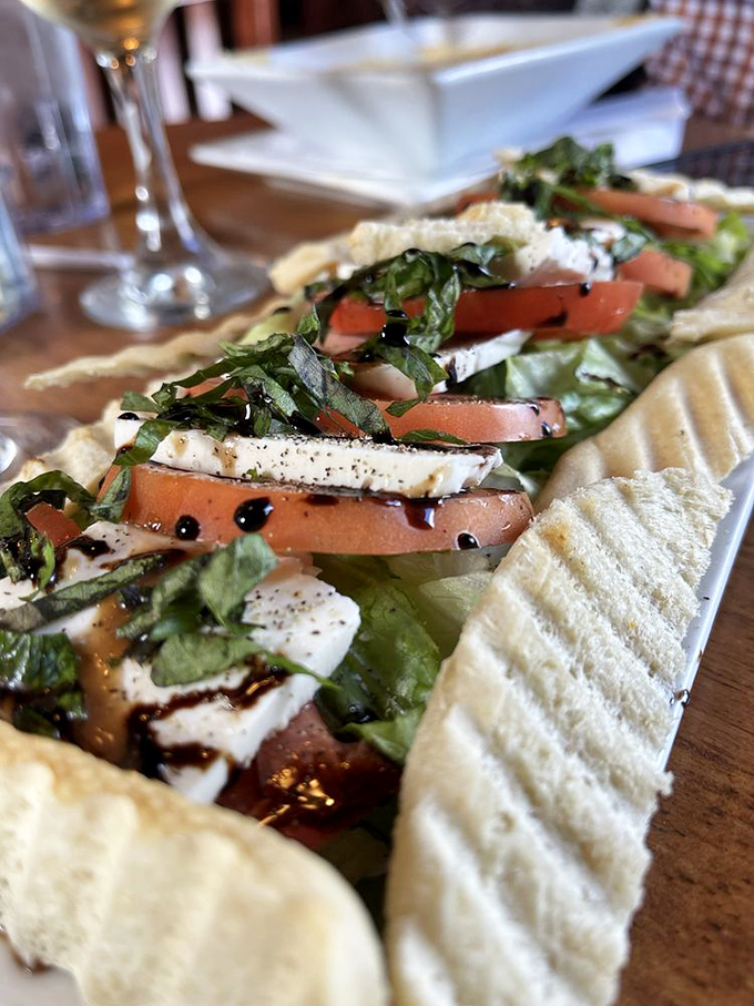 The Caprese salad arrives like edible Italian flag—red tomatoes, white mozzarella, green basil—a patriotic tribute to flavor that crosses all borders.