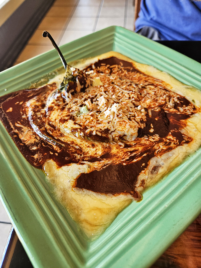 That green plate cradles what appears to be a chile relleno swimming in mole sauce—proof that sometimes the most delicious things aren't the most photogenic.