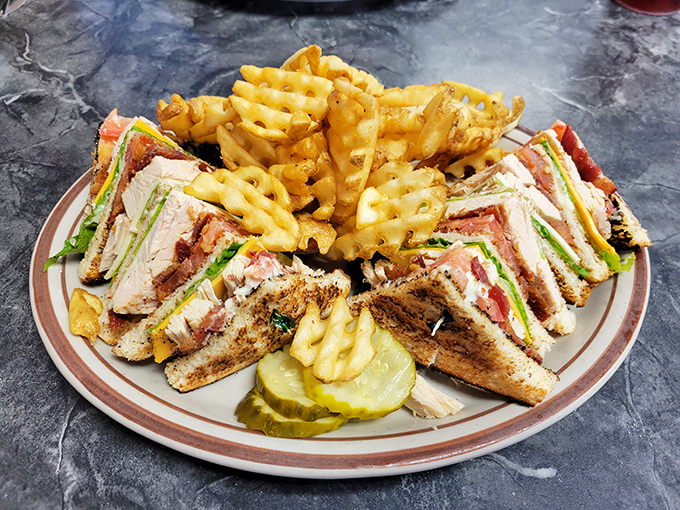 A club sandwich that doesn't need to show off—perfectly stacked layers of comfort between toasted bread with waffle fries that crunch loud enough to turn heads.