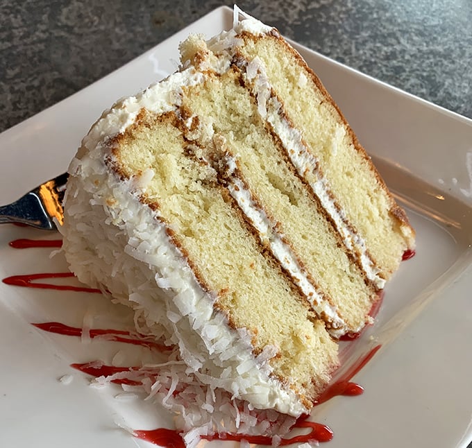 A slice of coconut cake that doesn't whisper "tropical vacation"&mdash;it belts it out like a Broadway finale, complete with dramatic raspberry sauce.