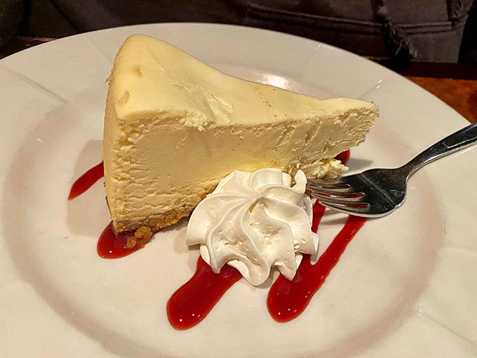 A slice of cheesecake so majestic it deserves its own ZIP code, with raspberry sauce adding that perfect sweet-tart counterpoint.