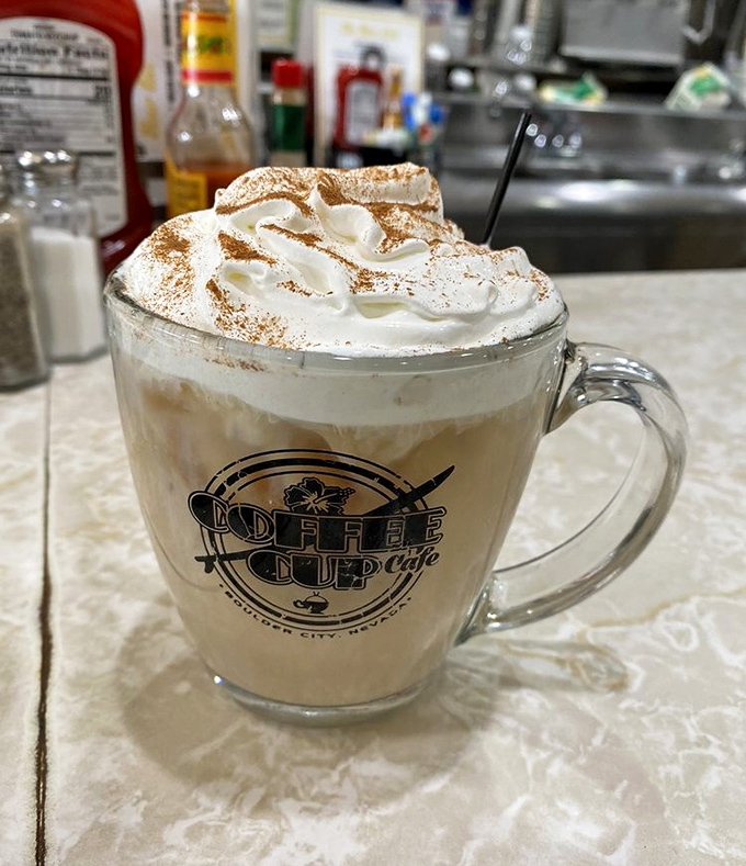Whipped cream mountain on coffee lake—a dessert disguised as a morning beverage. The logo mug makes it Instagram-official.