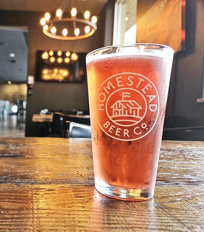 A perfectly poured craft beer sporting the Homestead logo &ndash; because pizza without beer is like Batman without Robin: still good, but missing its sidekick.