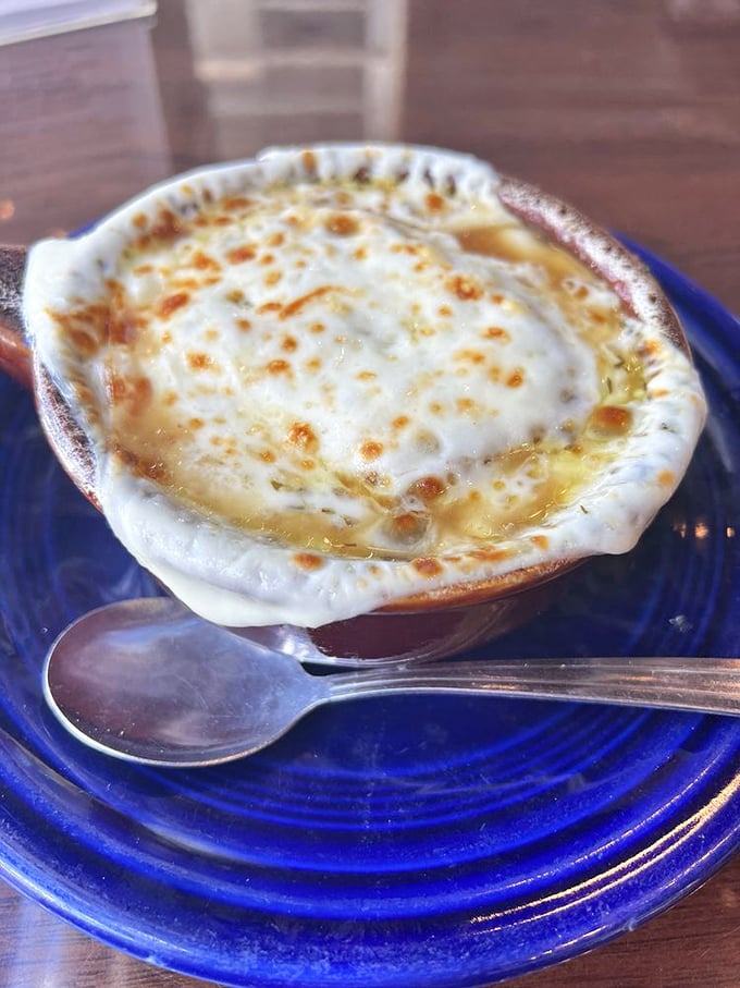 French onion soup wearing its cheese cap with pride&mdash;a bubbling masterpiece that's basically an edible hug in a blue ceramic crock.
