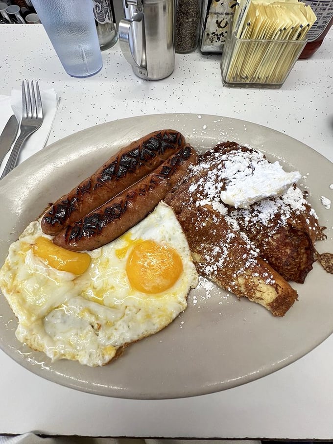 French toast and sausage links sharing a plate like old friends at a reunion. The powdered sugar isn't garnish&mdash;it's essential punctuation.