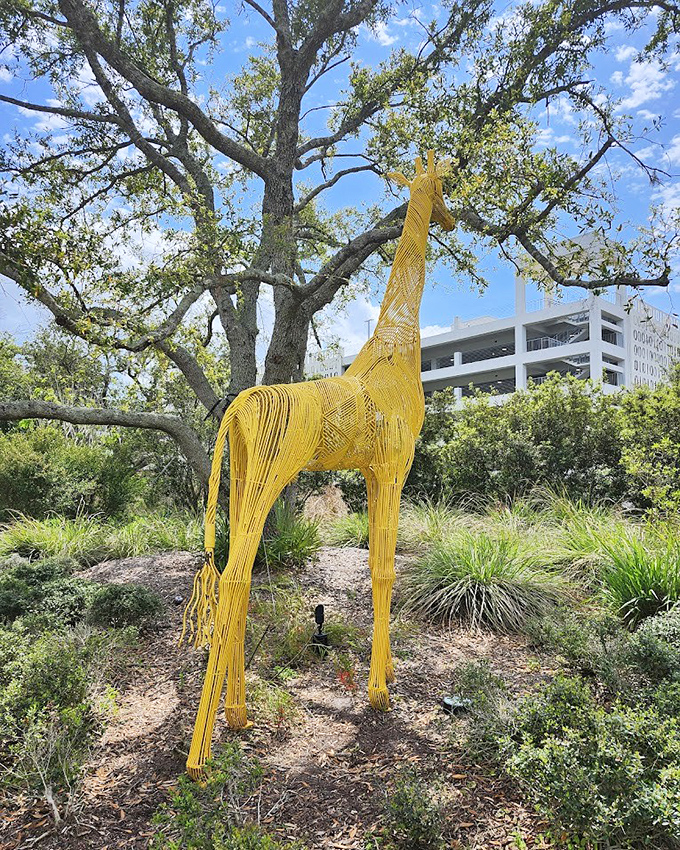 The whimsical yellow giraffe stretches toward the sky, its wire-frame construction creating a fascinating interplay of light and shadow throughout the day.