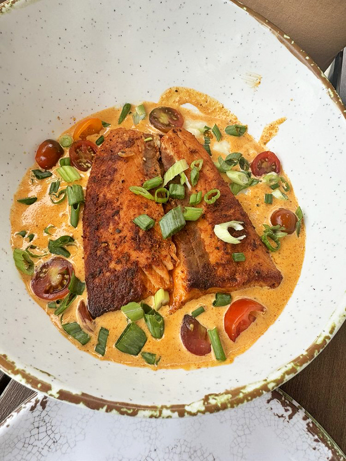 Blackened salmon lounging in a creamy pool of sauce, garnished with green onions and cherry tomatoes&mdash;like a spa day for your taste buds.