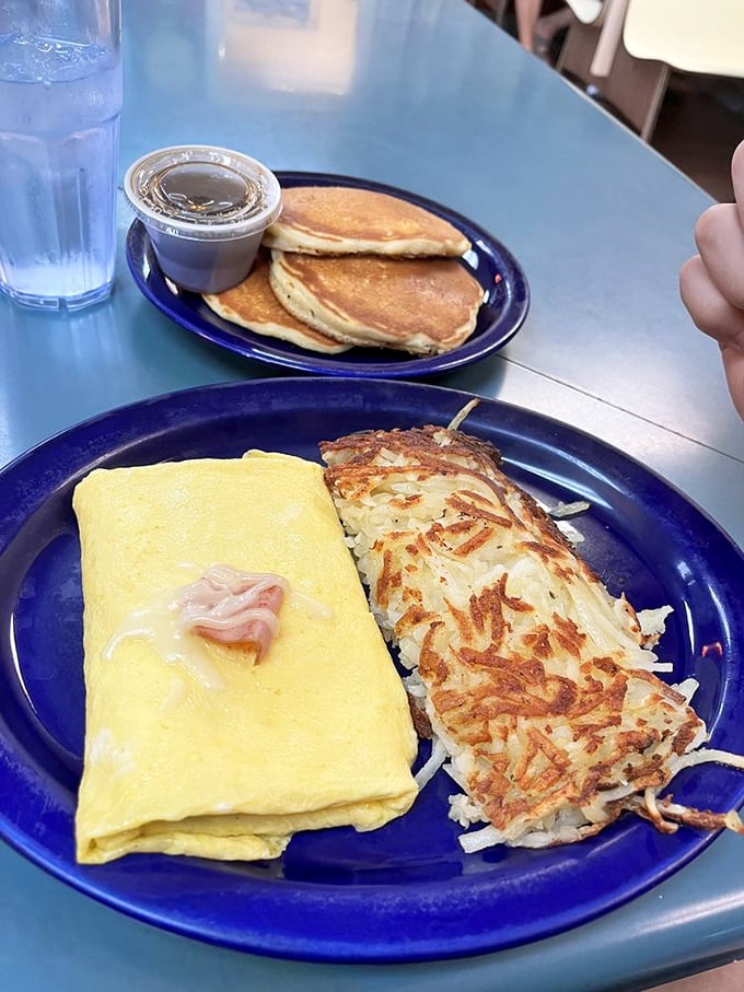 An omelet and hash browns that share a plate like old friends &ndash; one folded with care, the other crispy-edged and ready for fork exploration.