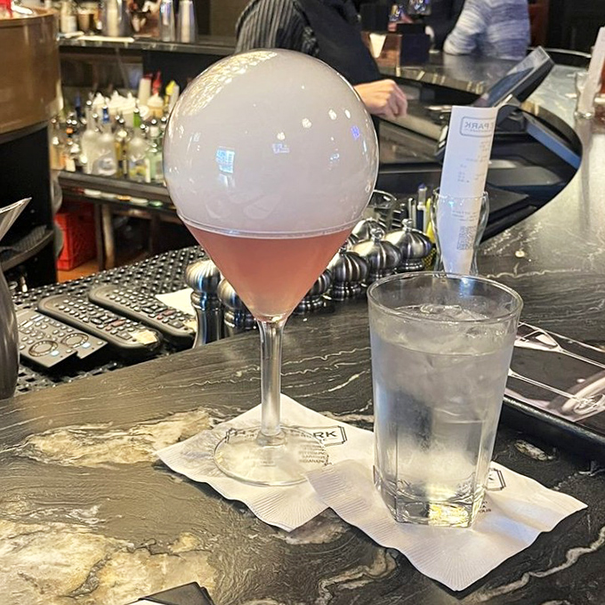 The hibiscus cosmo arrives under a dramatic dome, proving that at Hyde Park, even the cocktails know how to make a theatrical entrance.