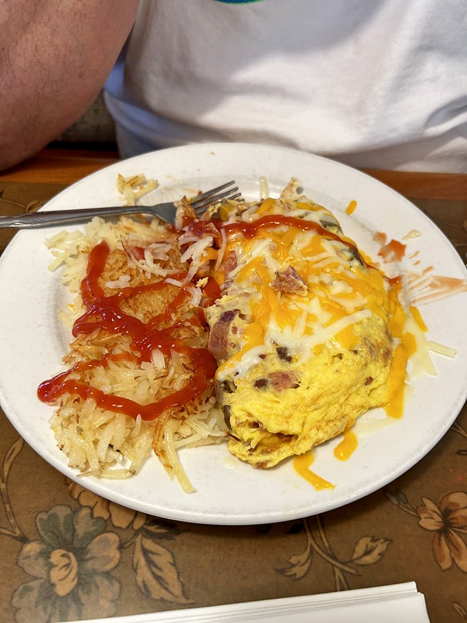 An omelet that's seen things—stuffed with savory treasures and blanketed in melted cheese, with hash browns standing by for moral support.