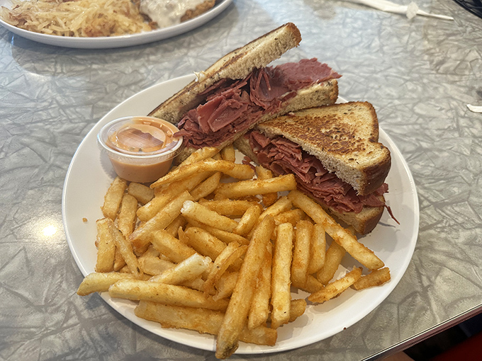 A pastrami sandwich so generous it requires strategic planning to eat. Those golden fries are no mere sidekick.