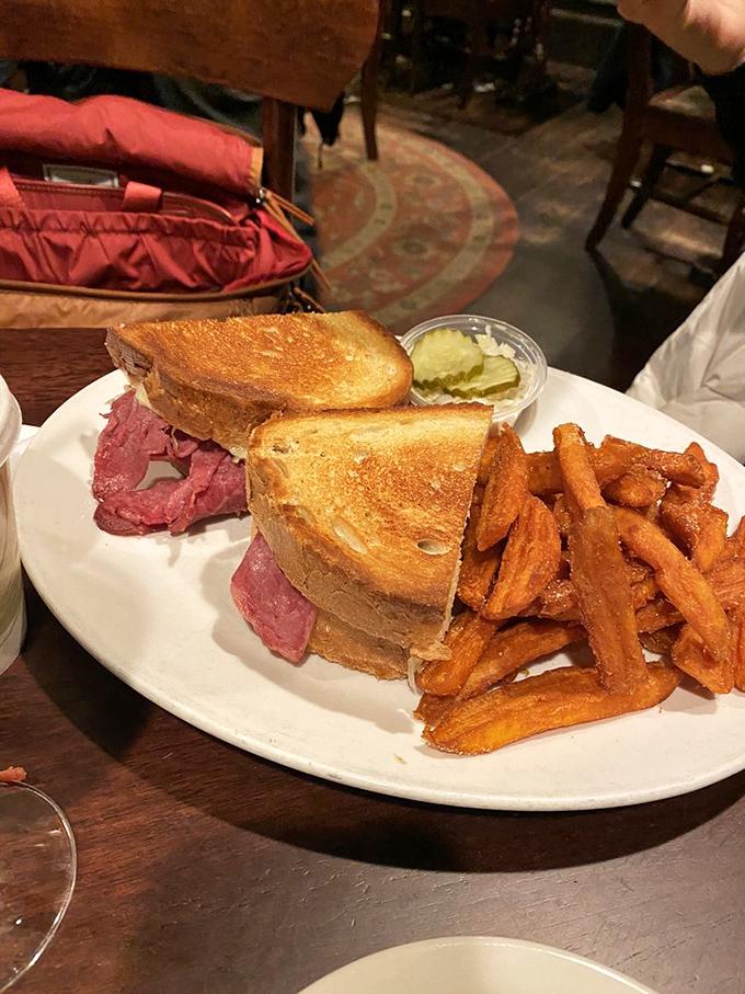 The Reuben sandwich stands tall and proud, with corned beef stacked so generously it requires jaw gymnastics and sweet potato fries that demand equal attention.