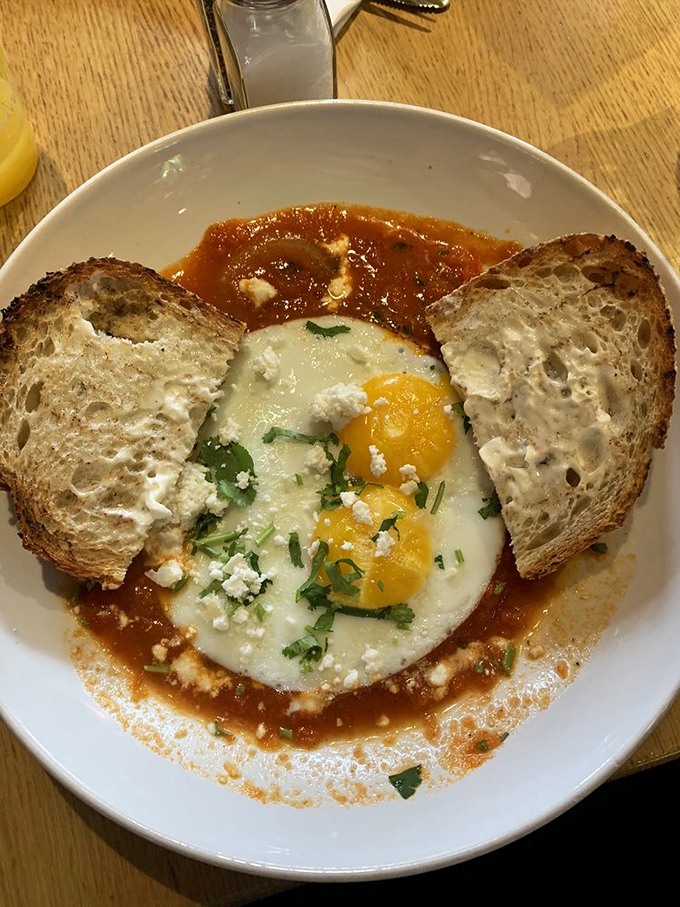 A sunny-side-up egg floats in a sea of tomato sauce with crusty bread standing by, ready for the delicious dipping expedition ahead.