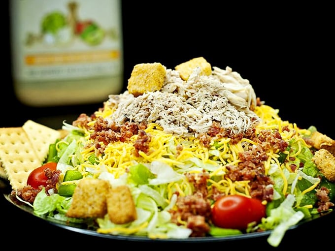 This towering salad situation involves tortilla chips, meat, cheese, and vegetables having an excellent party together.