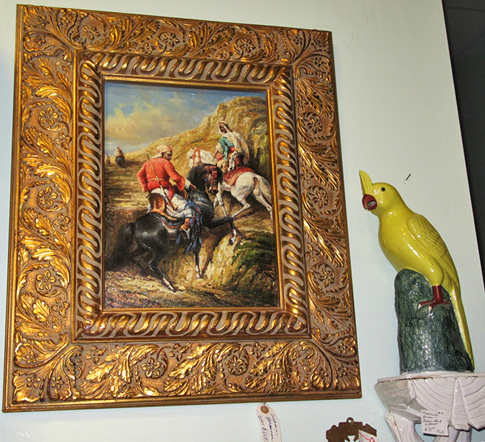 Art meets whimsy as an ornate gold-framed painting shares wall space with a cheerful yellow bird figurine &ndash; unexpected neighbors in the antique world.