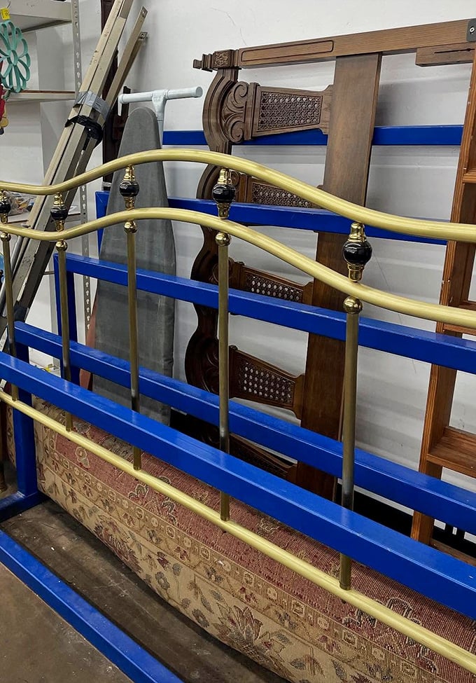 Brass bed frames and wooden headboards stacked like a game of architectural Jenga &ndash; someone's dream bedroom waiting to be assembled.