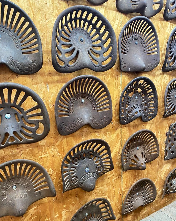 Wall of cast-iron tractor seats &ndash; practical farm equipment transformed into industrial art. Comfort was clearly optional back then.