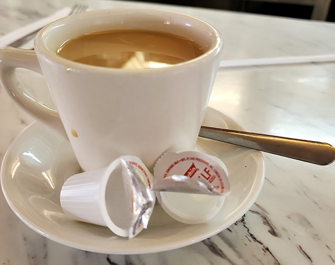 Coffee served in a proper mug with those tiny creamer cups that somehow make the experience feel more authentic and satisfying.