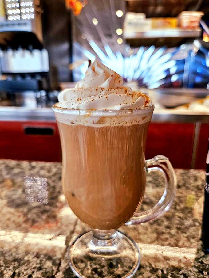Coffee elevated to dessert status—a frothy, cinnamon-dusted cloud floating atop liquid motivation, served in a glass mug that lets you appreciate the artistry before the caffeine kicks in.