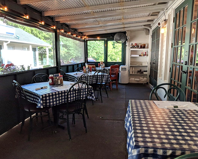 The screened porch dining area offers a breezy Southern experience. Those blue checkered tablecloths aren't just decoration &ndash; they're a promise of good things to come.