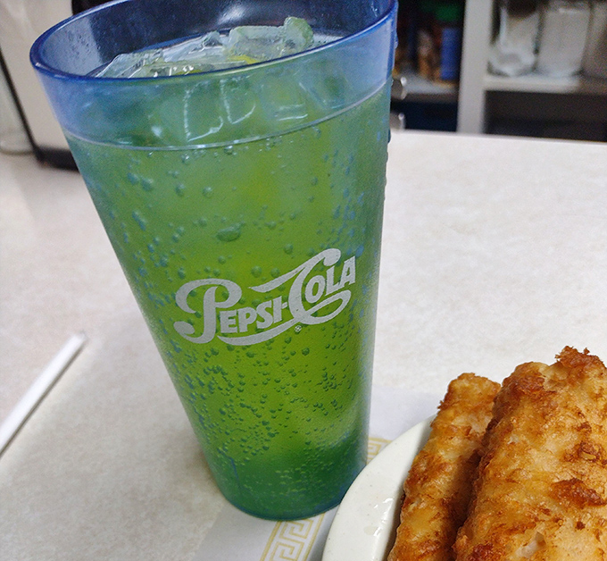 That electric green Pepsi-Cola cup brings back childhood memories. Paired with what appears to be a golden-fried treasure &ndash; hydration and happiness on a table.