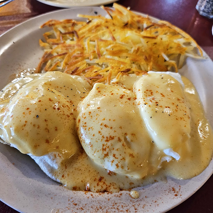 Eggs Benedict done diner-style &ndash; perfectly poached eggs nestled on English muffins, blanketed in hollandaise with crispy hash browns standing guard.