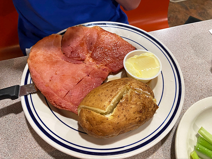 Ham steak so generous it's practically hanging off the plate, with a baked potato standing by for moral support.