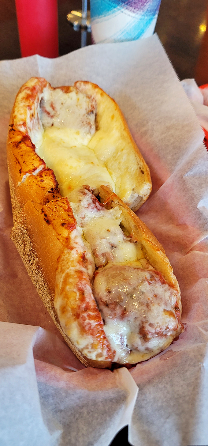 Behold the meatball sub in its natural habitat—swimming in melted cheese and ready to ruin any shirt worth sacrificing.