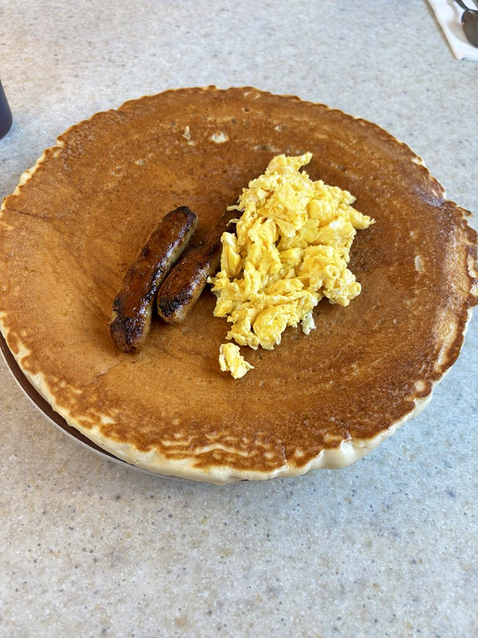 A pancake so perfectly browned it deserves its own Instagram account, topped with scrambled eggs and sausage links that mean business.