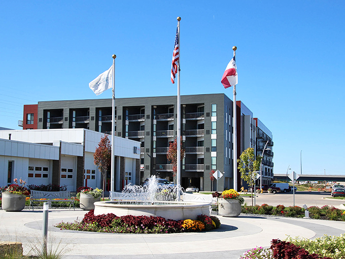 A sunny day in Bettendorf where modern architecture, a flowing fountain, and vibrant flowers create a welcoming and lively atmosphere.